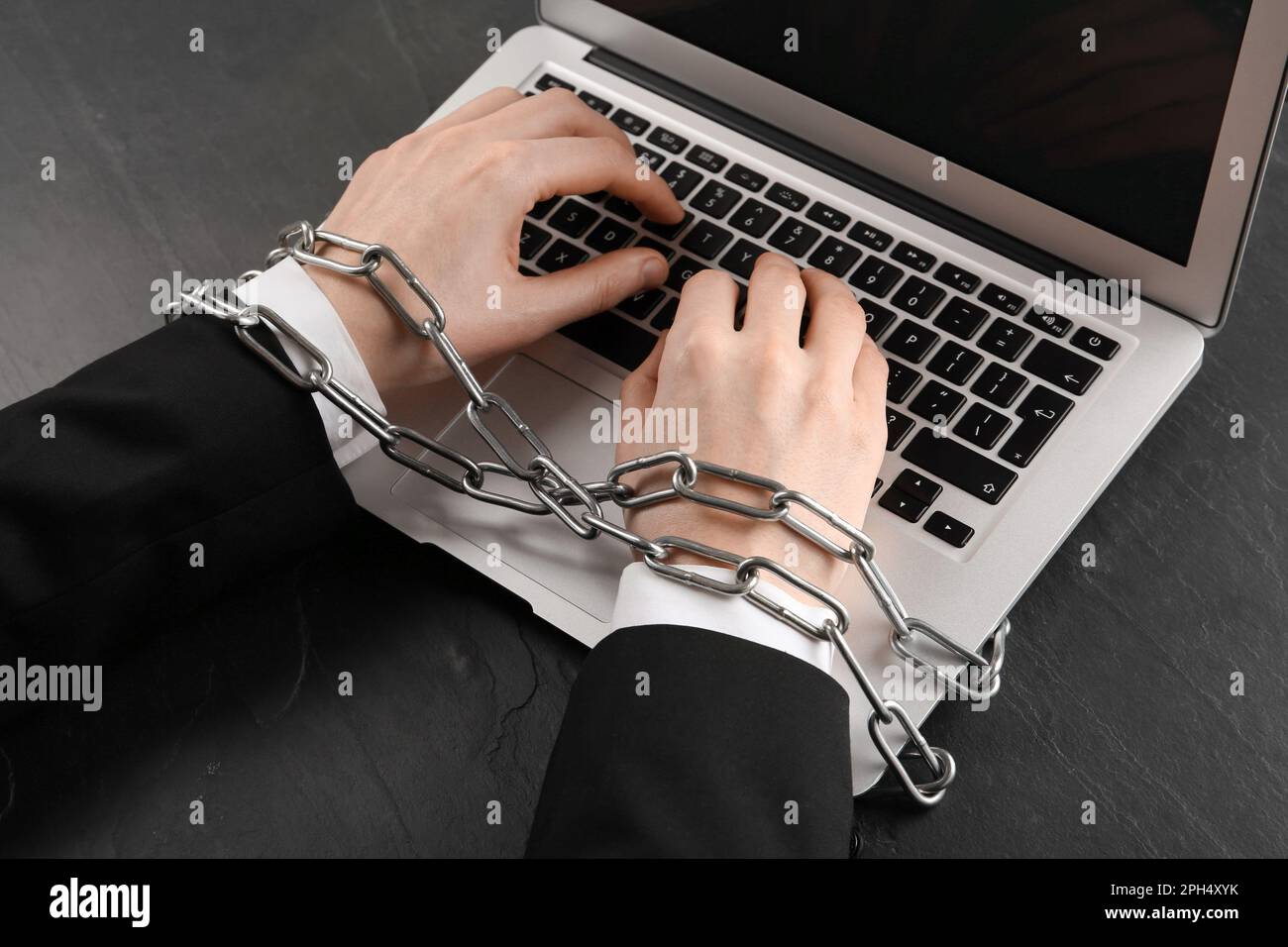 Internet addiction. Man typing on laptop with chained hands at black ...