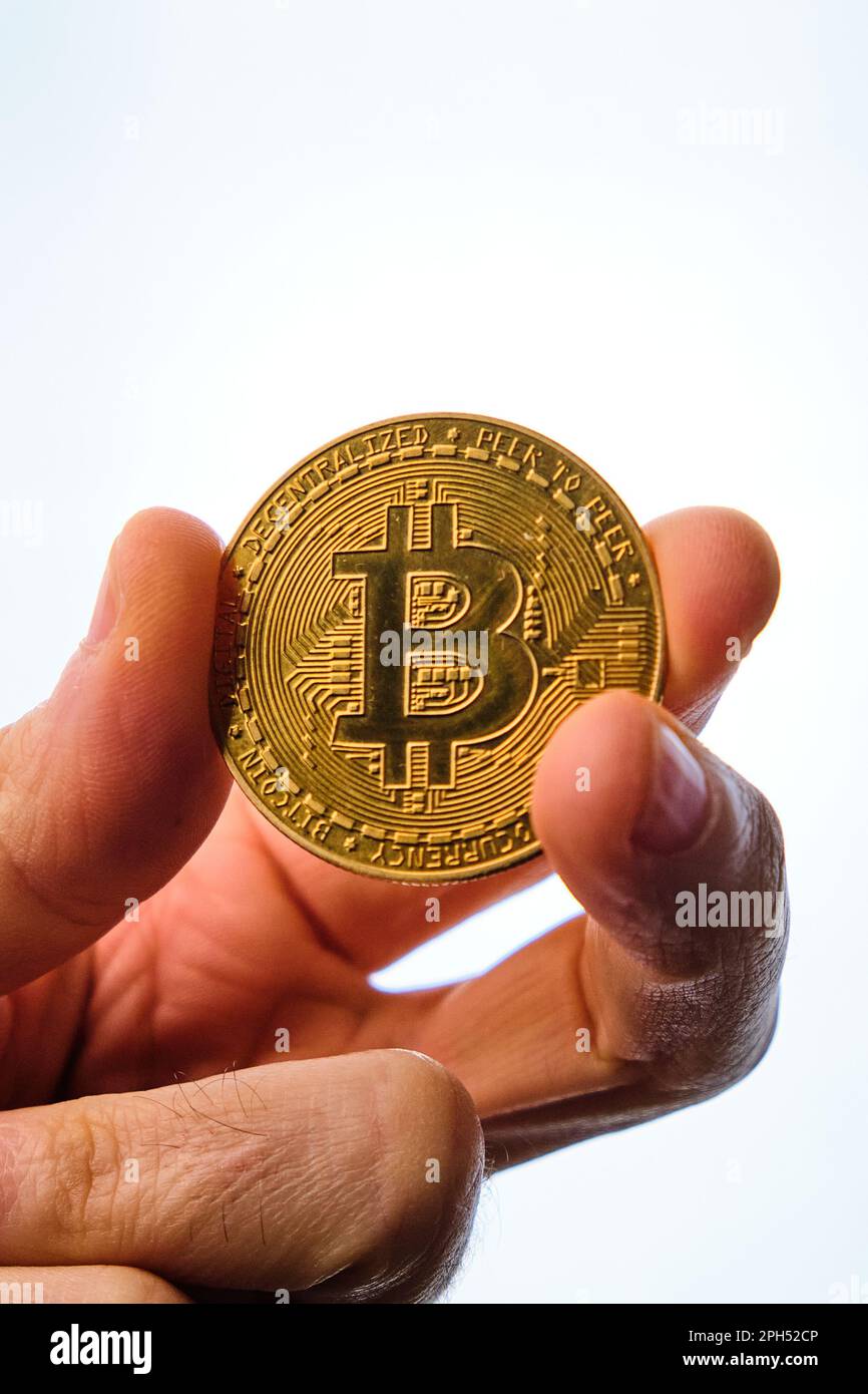 Man's hand holding a bitcoin coin with three fingers, on a white ...