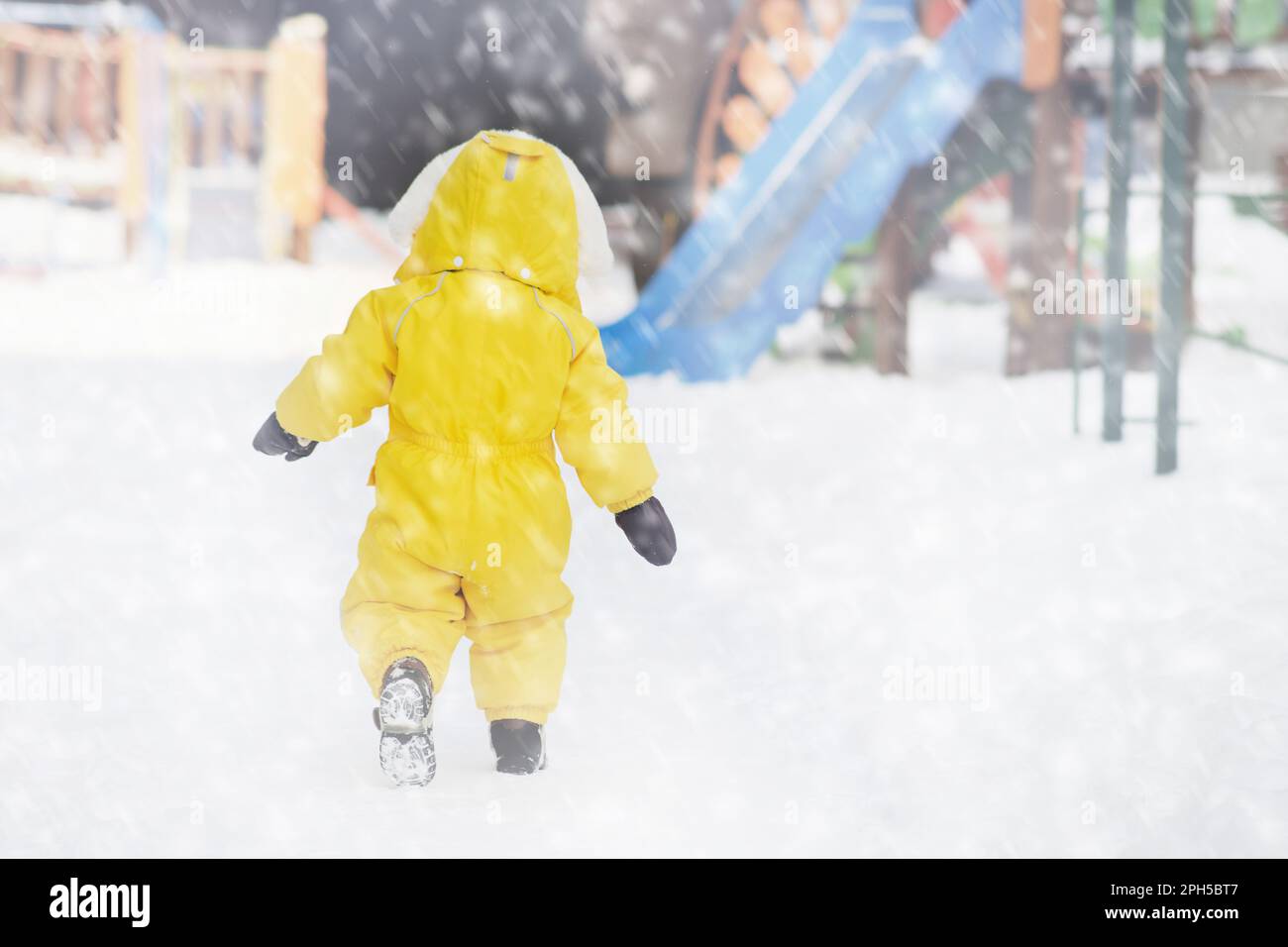 Toddler baby runs through the snow to play on the winter playground ...