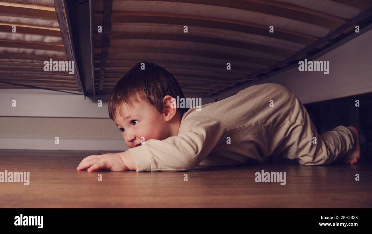 Toddler baby crawls and hides under the bed. Child climbed under the ...