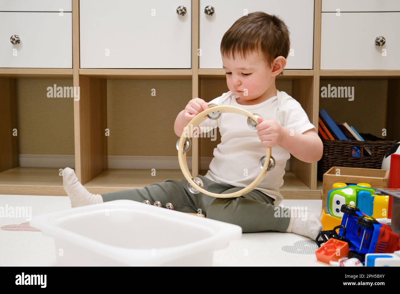 Toddler baby plays the tambourine while sitting on the floor in the ...