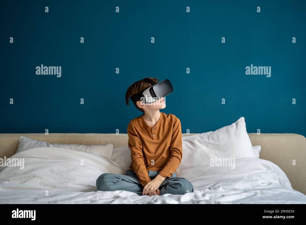 Interested schoolboy sit on bed look in 3D virtual reality glasses for ...