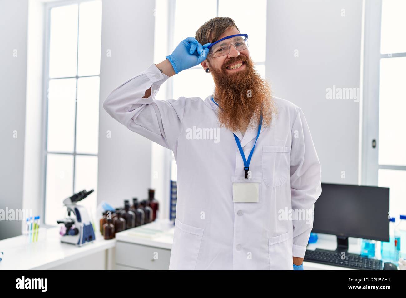 Young redhead man wearing scientist uniform standing at laboratory ...