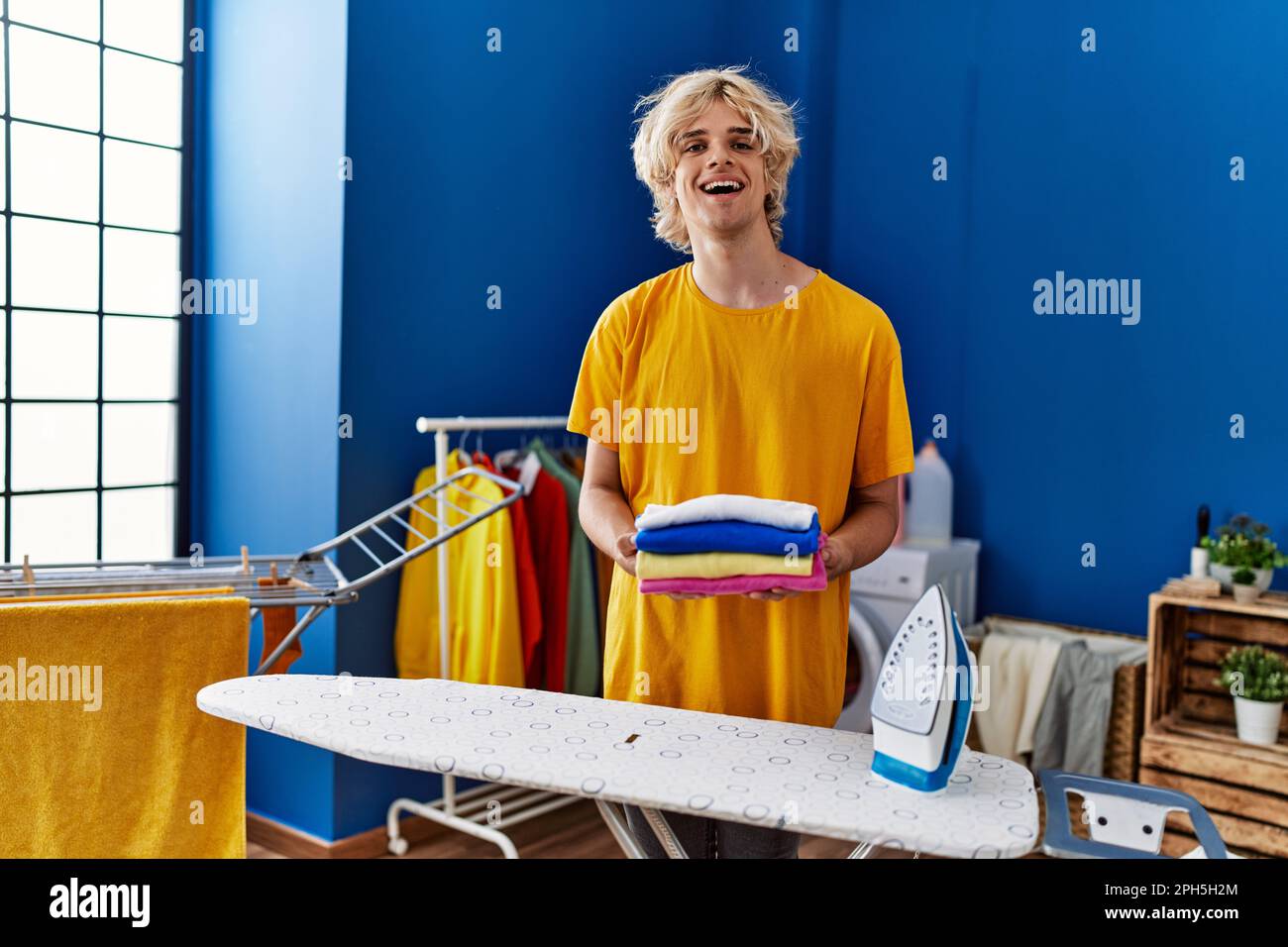 Young man ironing clothes at home smiling with a happy and cool smile ...