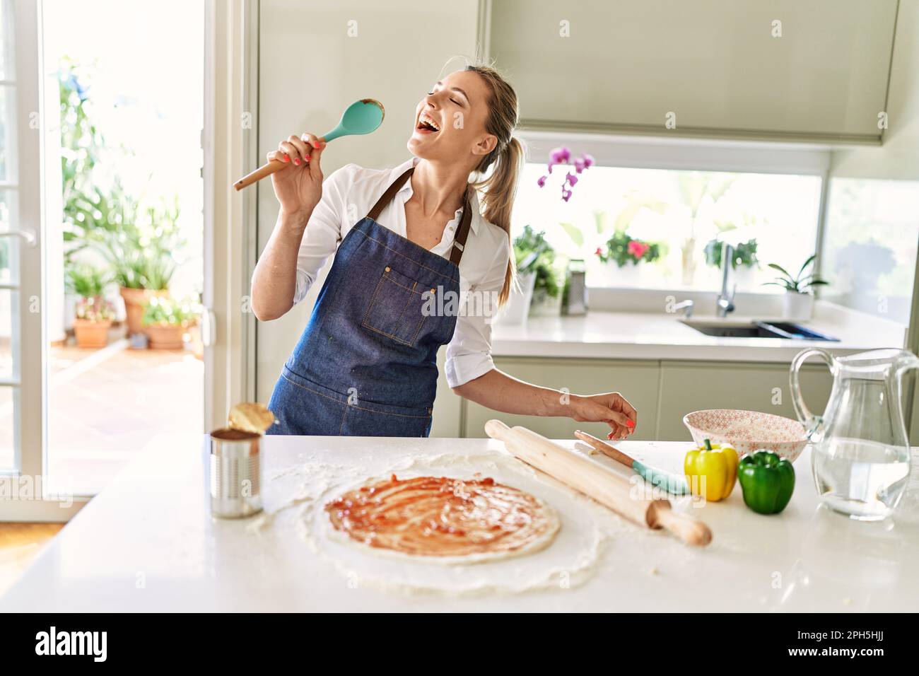 Young blonde woman singing song using spoon as a microphone cooking ...