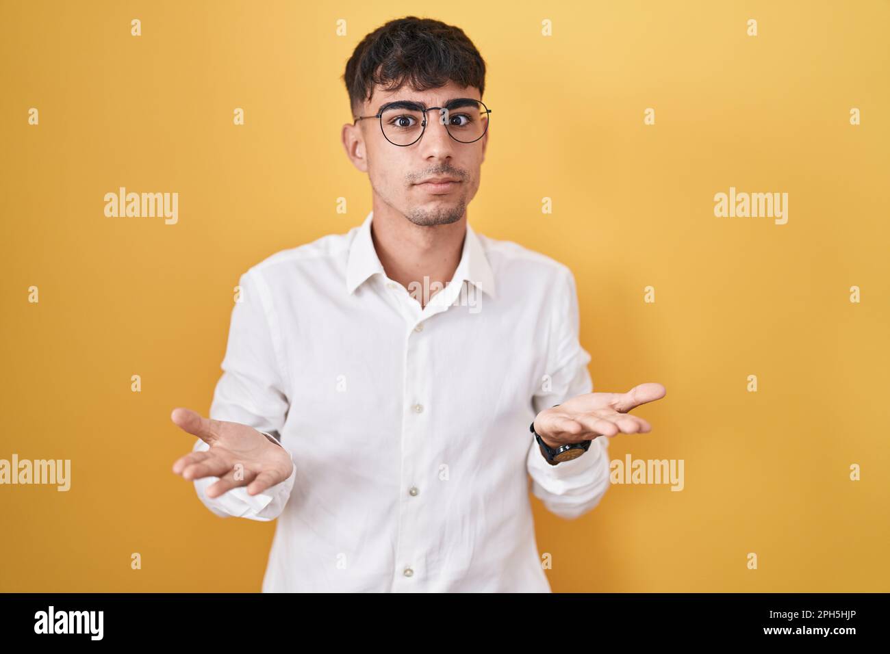 Young hispanic man standing over yellow background clueless and ...
