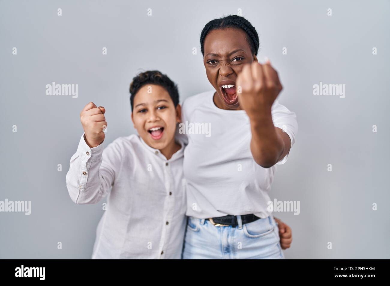 Young mother and son standing together over white background angry and ...