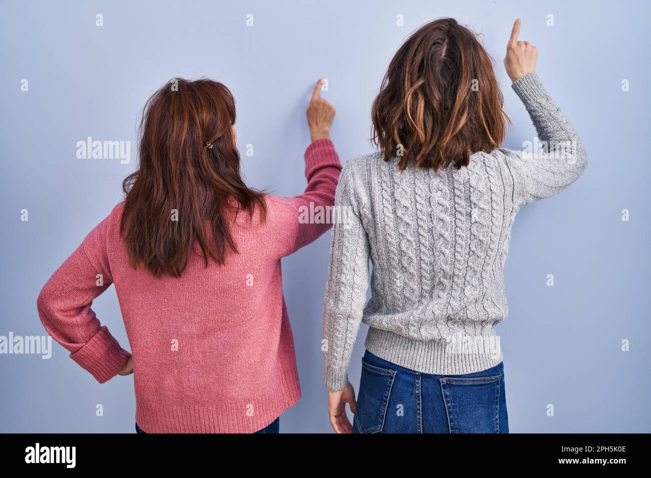 Mother and daughter standing over blue background posing backwards ...