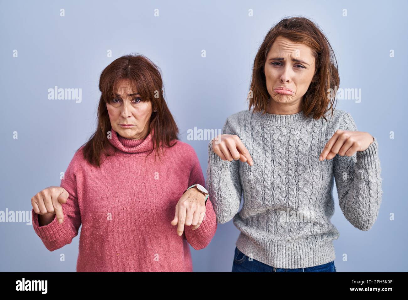 Mother and daughter standing over blue background pointing down looking ...