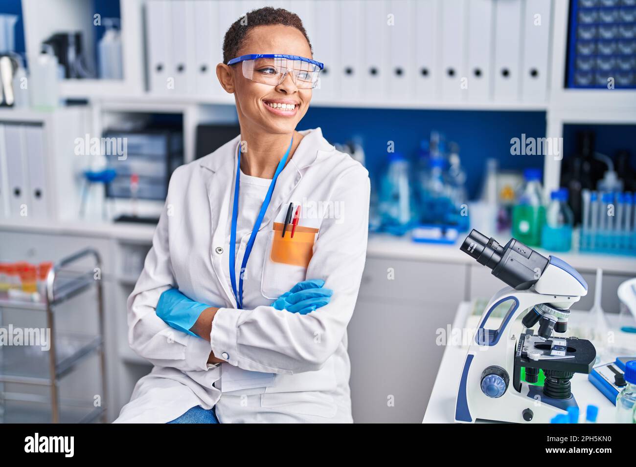 African american woman scientist smiling confident sitting with arms crossed gesture at ...