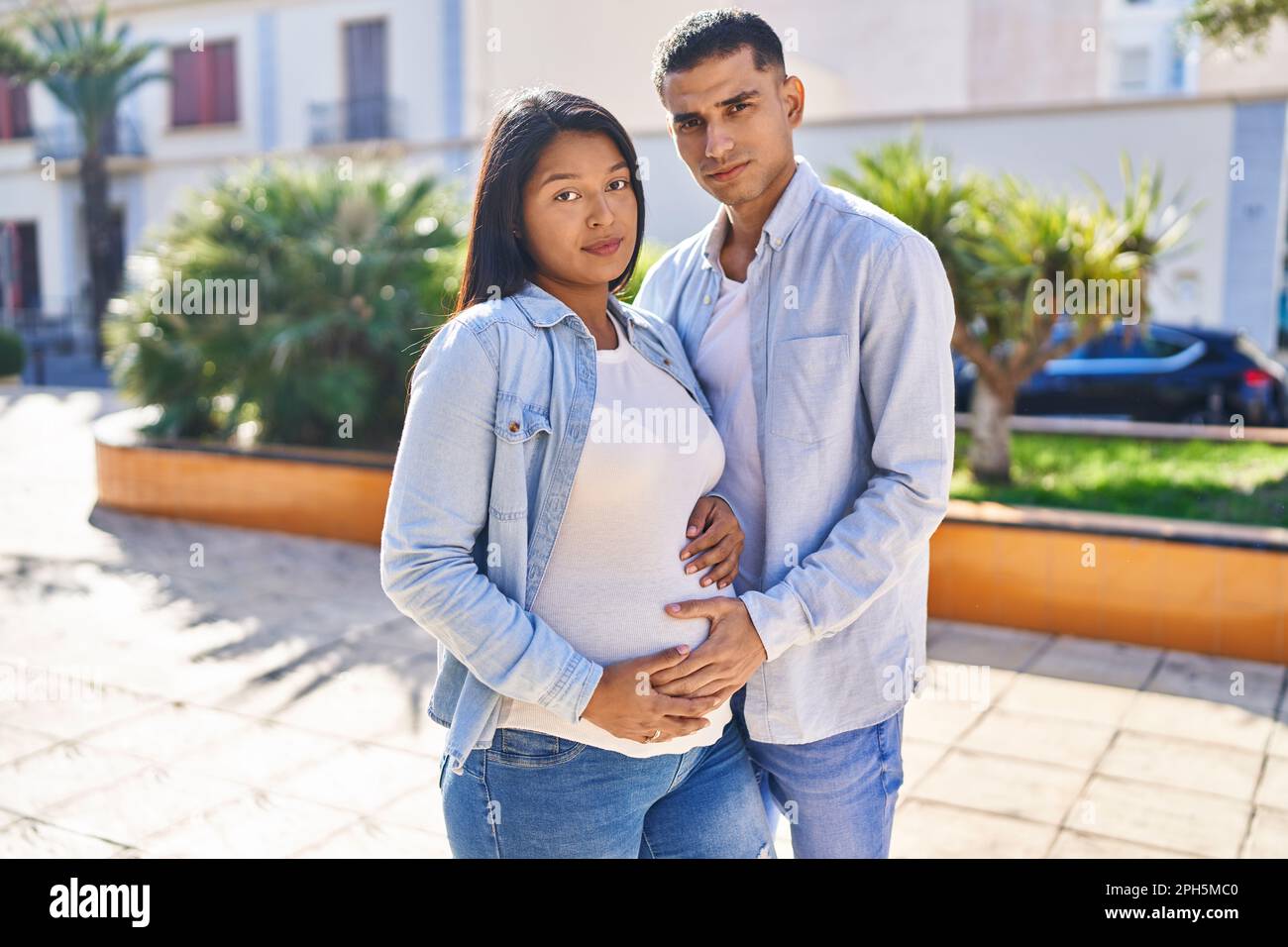 Young latin couple expecting baby hugging each other standing at park Stock Photo - Alamy