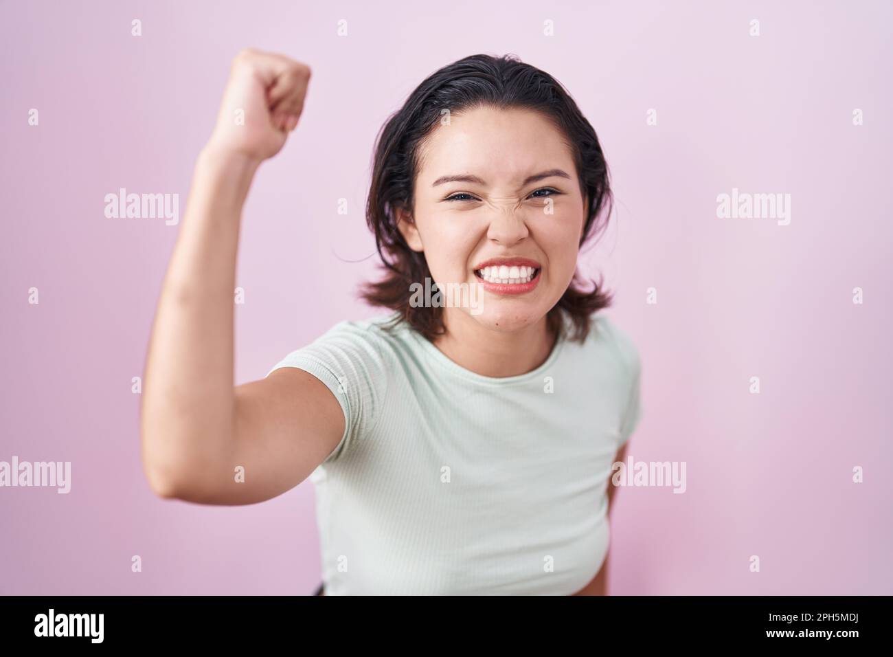 Hispanic young woman standing over pink background angry and mad ...