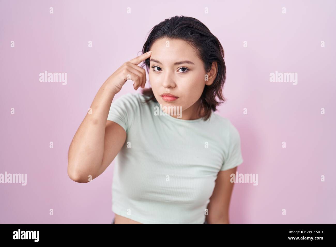 Hispanic young woman standing over pink background pointing unhappy to ...
