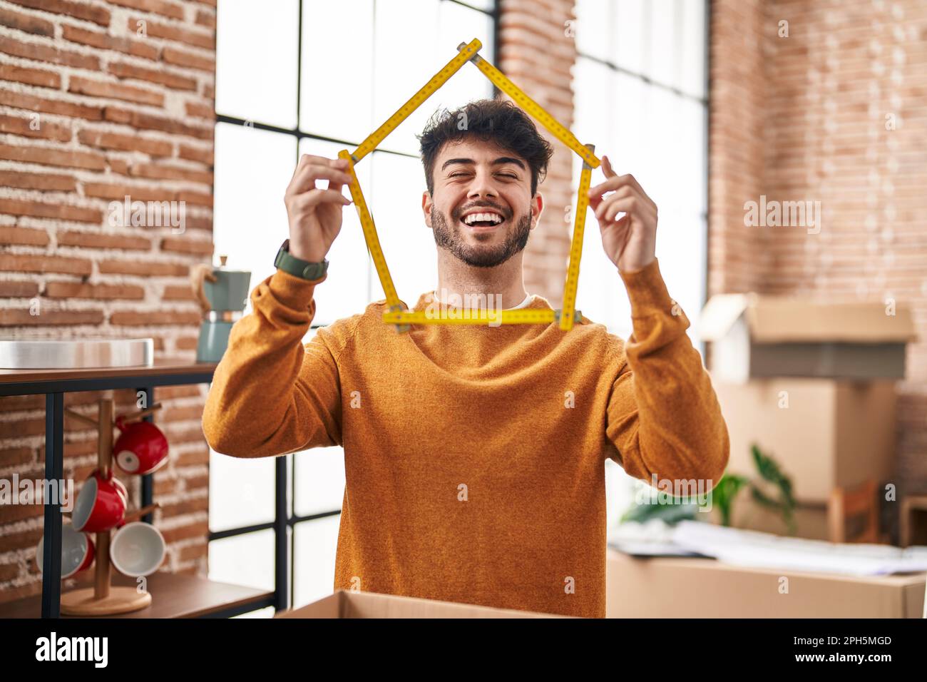 Hispanic man with beard moving to a new home holding ruler celebrating ...