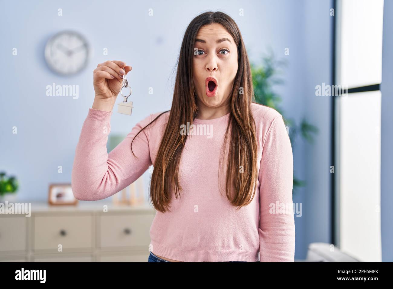 Young brunette woman holding keys of new home scared and amazed with ...