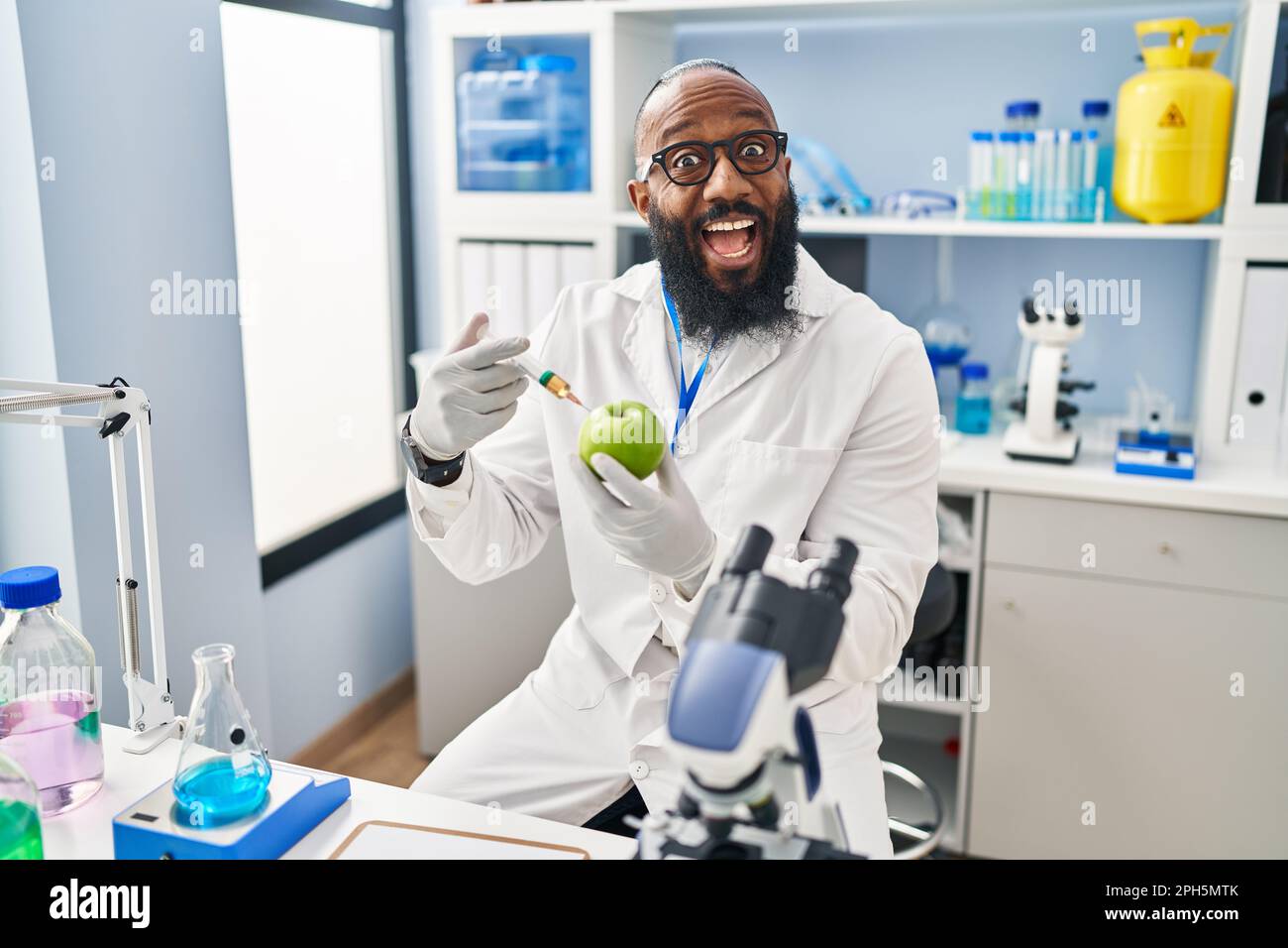 African american man working at scientist laboratory with apple celebrating crazy and amazed for ...