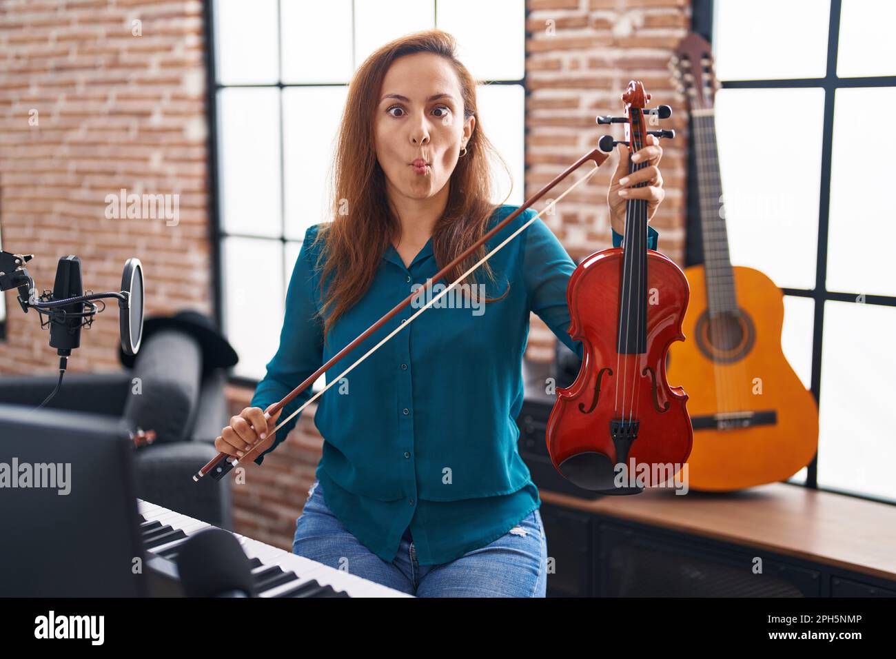 Brunette woman playing violin making fish face with mouth and squinting ...