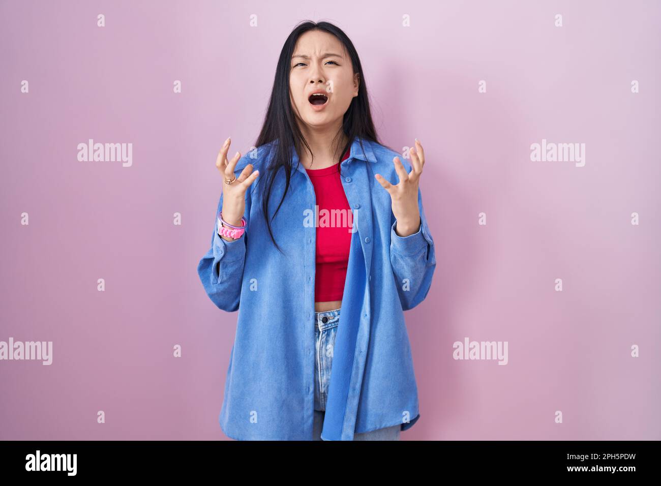 Young asian woman standing over pink background crazy and mad shouting ...