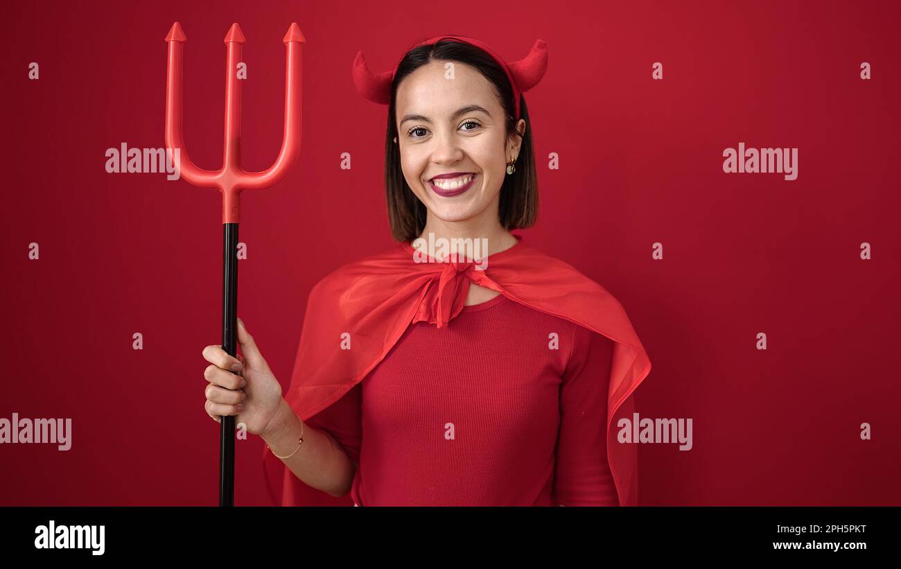 Young beautiful hispanic woman wearing devil costume holding trident ...