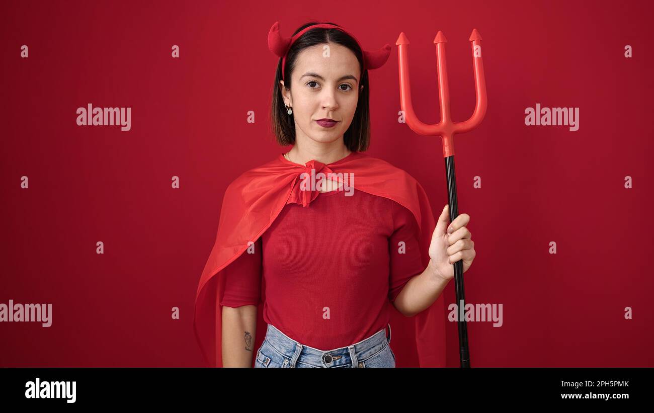 Young beautiful hispanic woman wearing devil costume holding trident ...