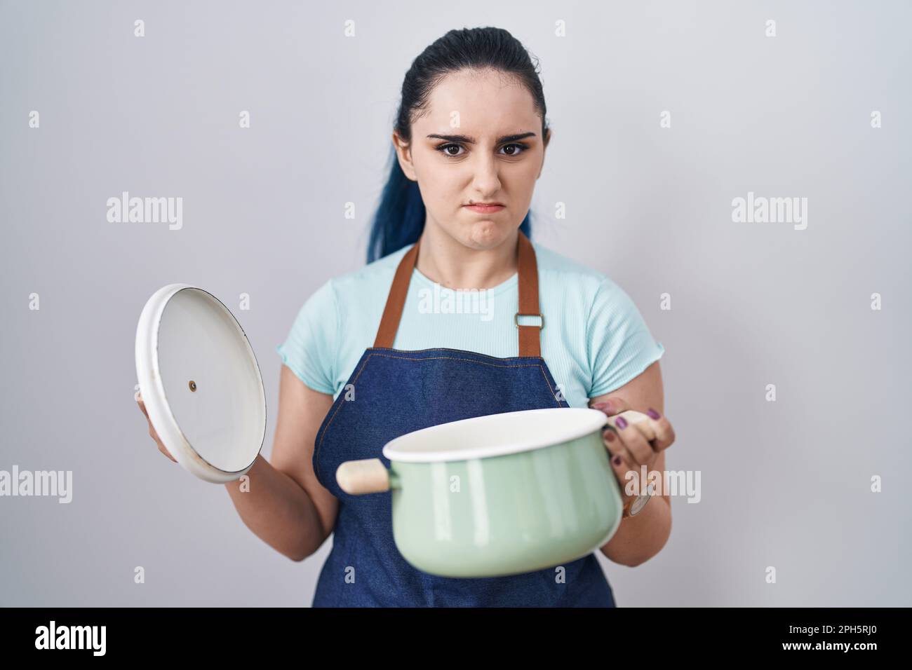 Young modern girl with blue hair wearing apron holding cooking pot ...
