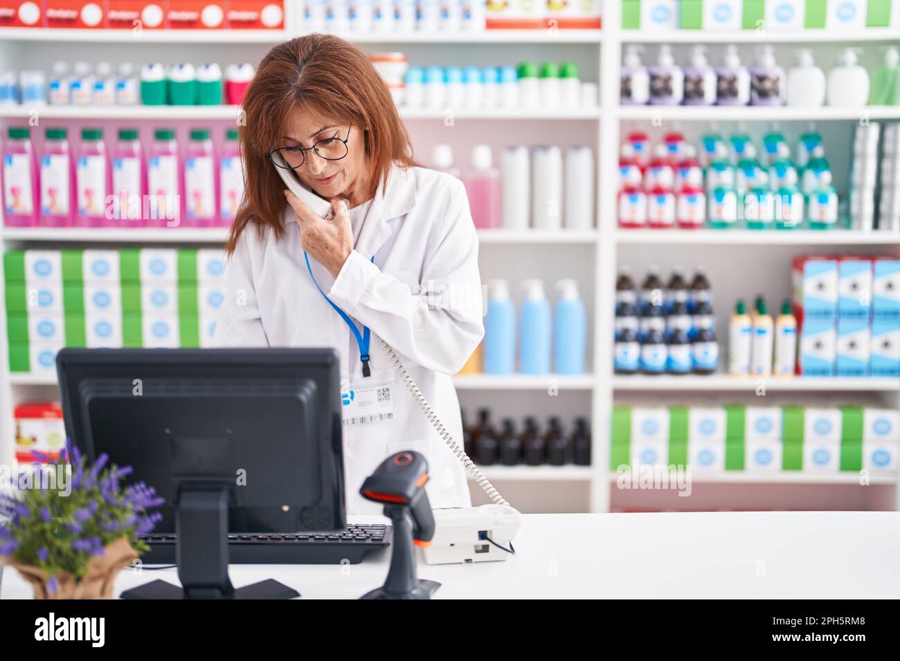 Middle age woman pharmacist talking on telephone using computer at ...