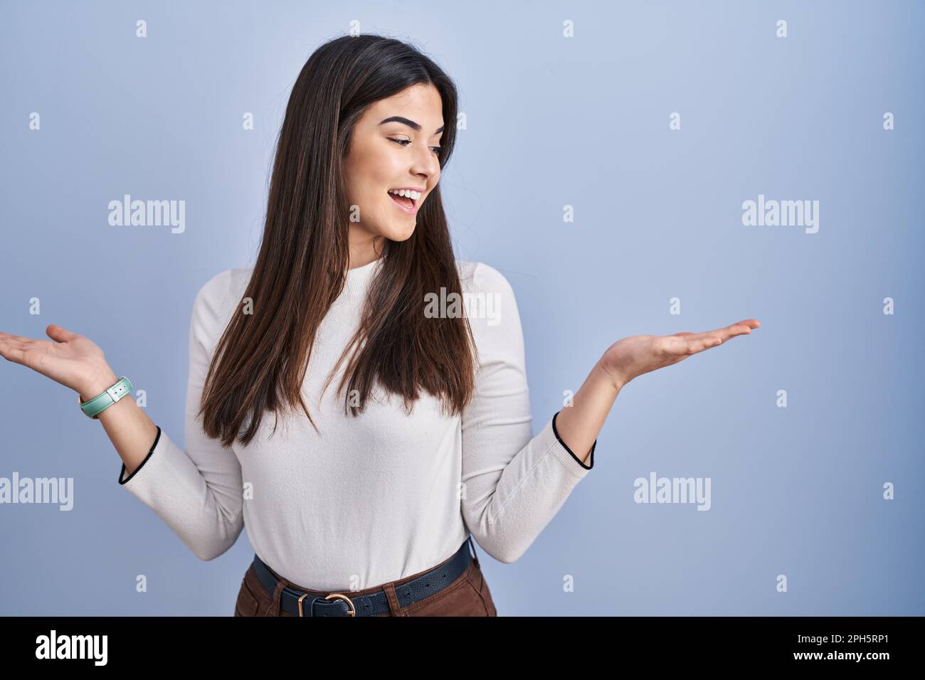 Young brunette woman standing over blue background smiling showing both ...