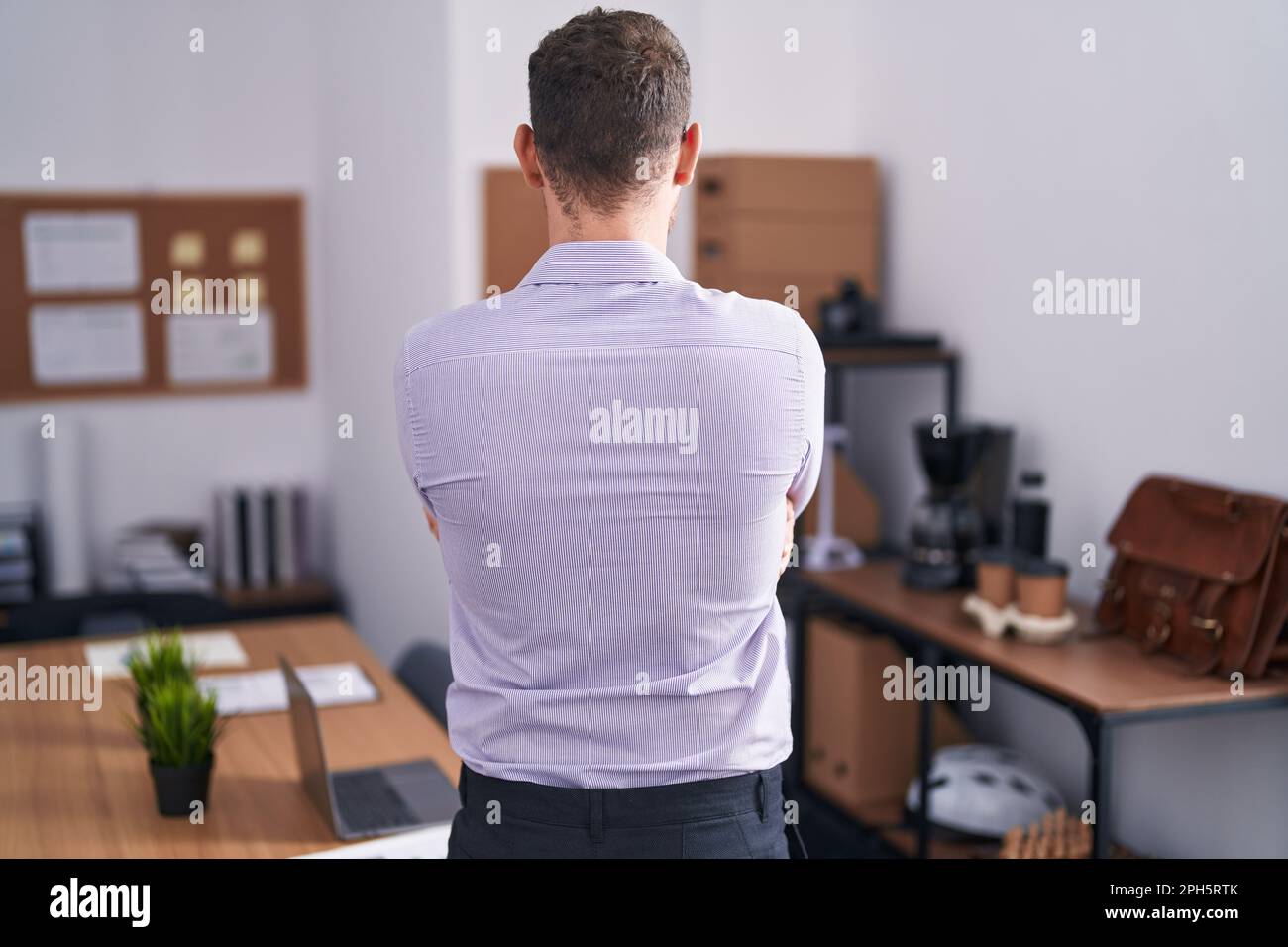 Young hispanic man at the office standing backwards looking away with ...
