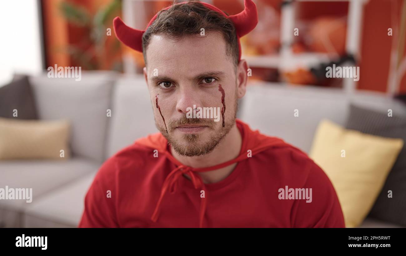 Young caucasian man wearing devil costume sitting on the sofa at home ...