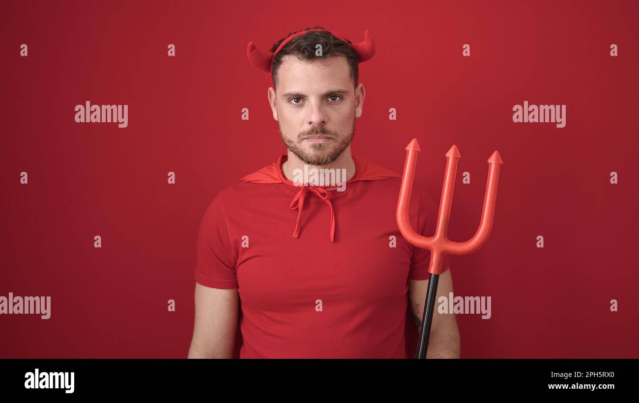 Young caucasian man standing with serious expression wearing devil ...