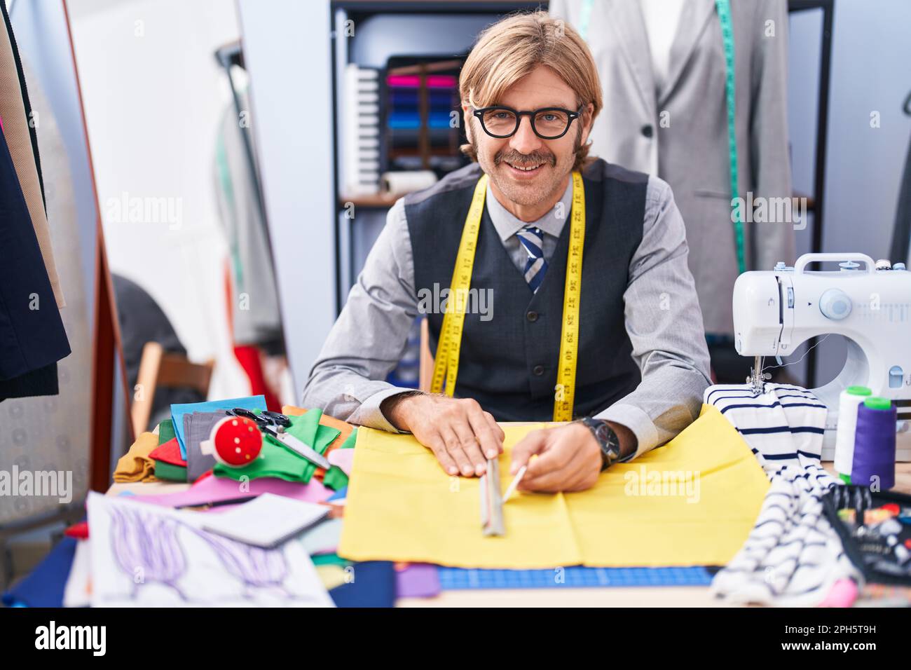 Young blond man tailor smiling confident make mark on cloth at clothing ...