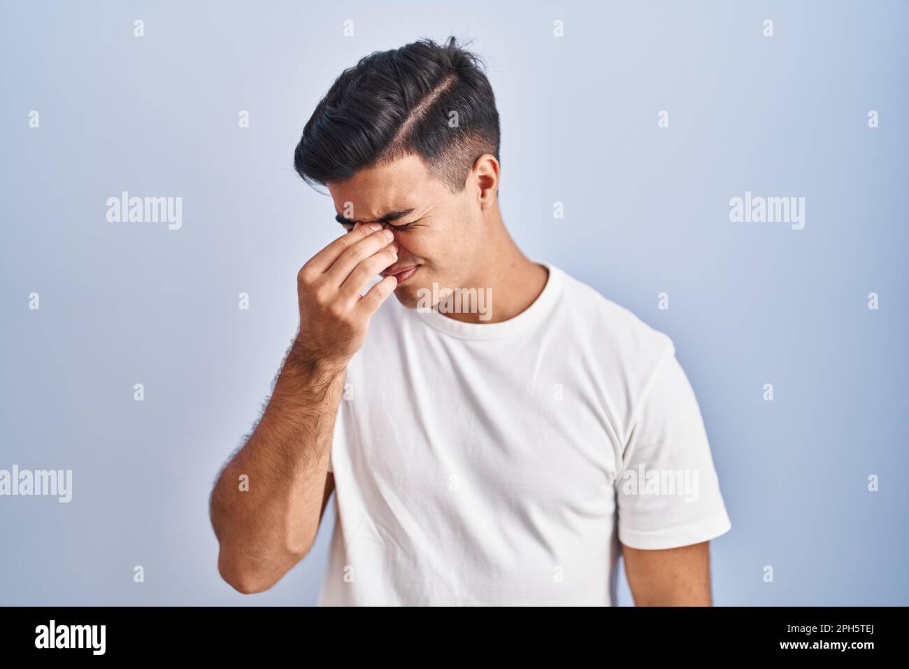 Hispanic man standing over blue background tired rubbing nose and eyes ...