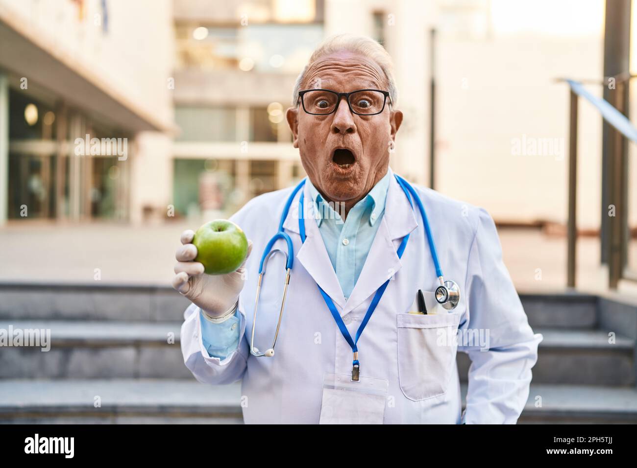 Senior doctor with grey hair holding healthy green apple scared and ...