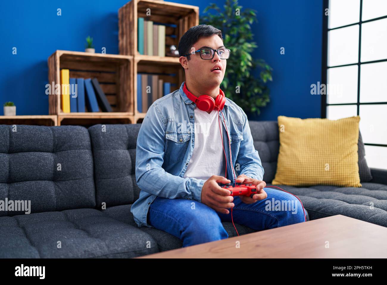 Down syndrome man playing video game sitting on sofa at home Stock ...