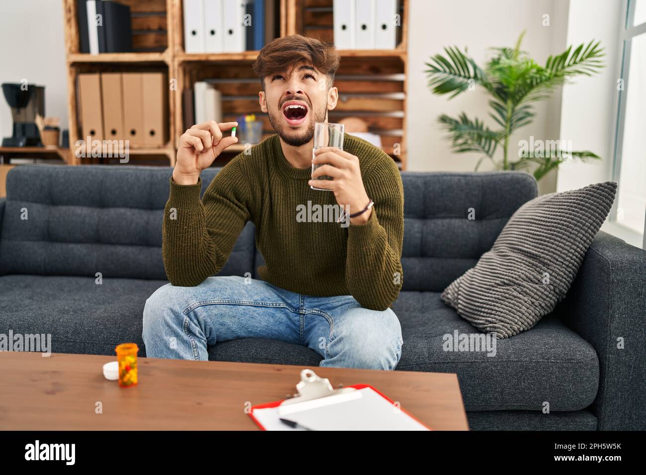 Arab man with beard working on depression holding pills and water angry ...