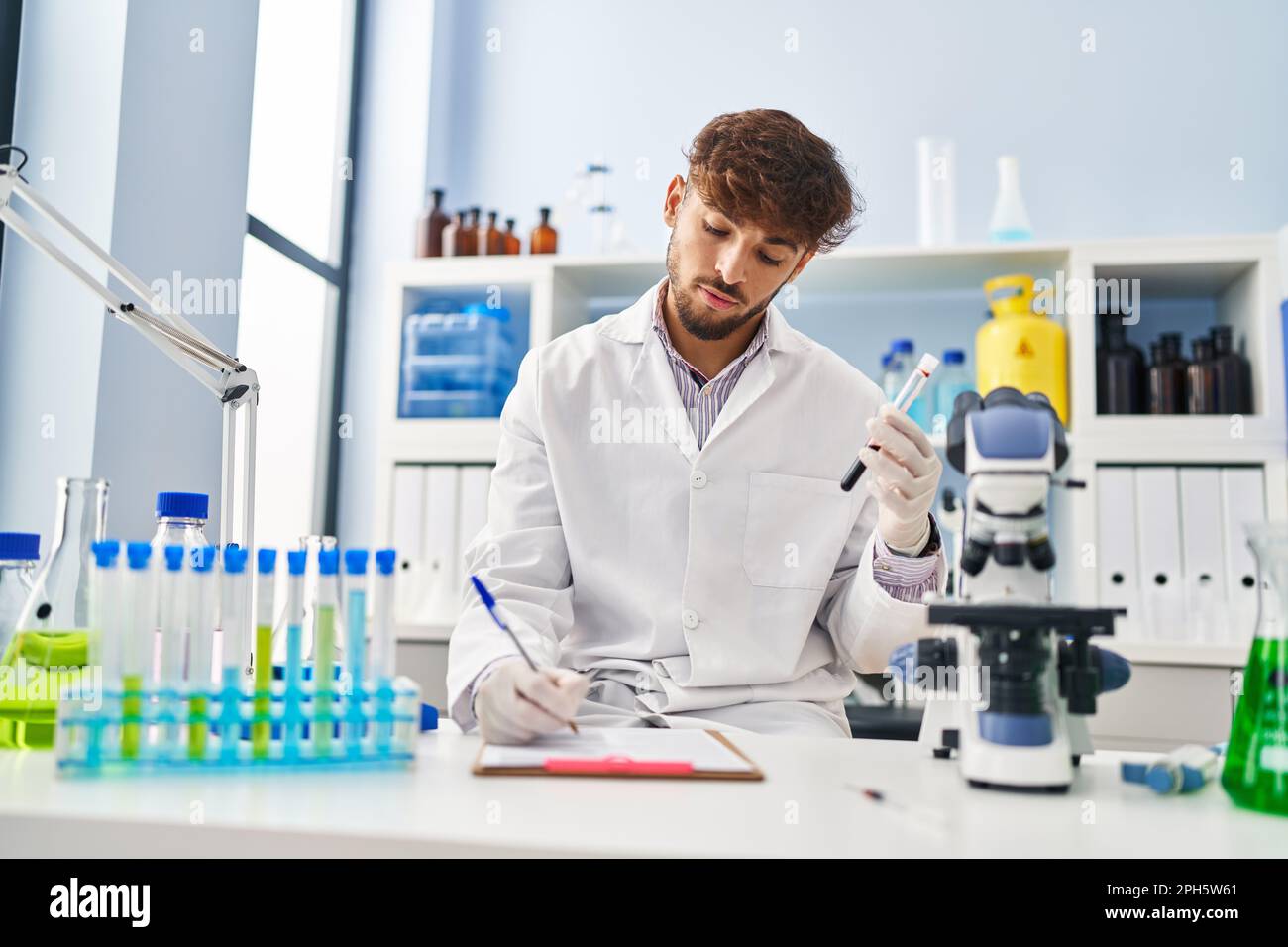 Young arab man scientist write on document analysing blood test tube at ...