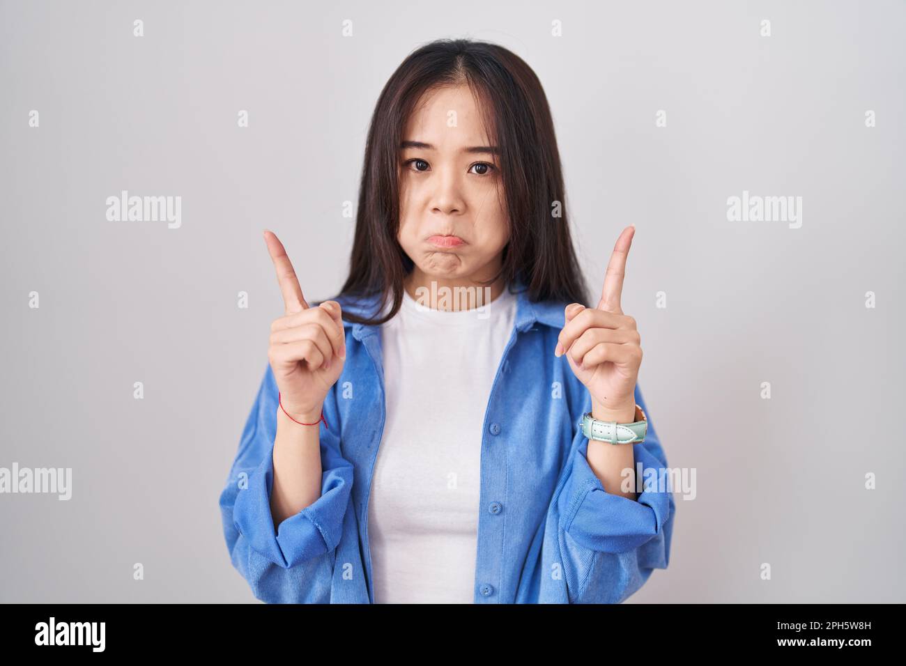 Young chinese woman standing over white background pointing up looking ...