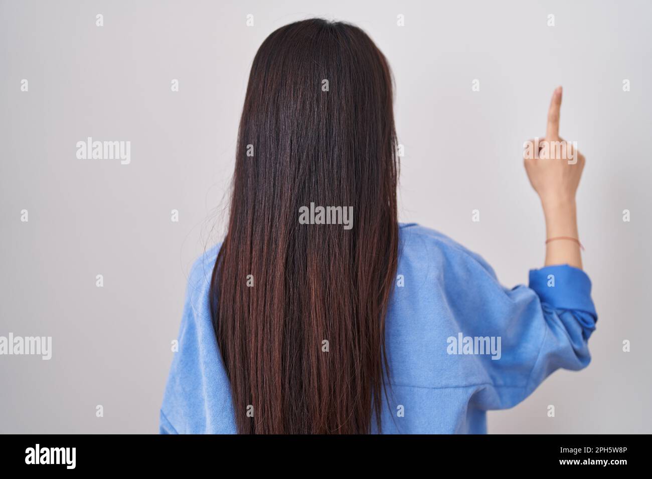 Young chinese woman standing over white background posing backwards ...