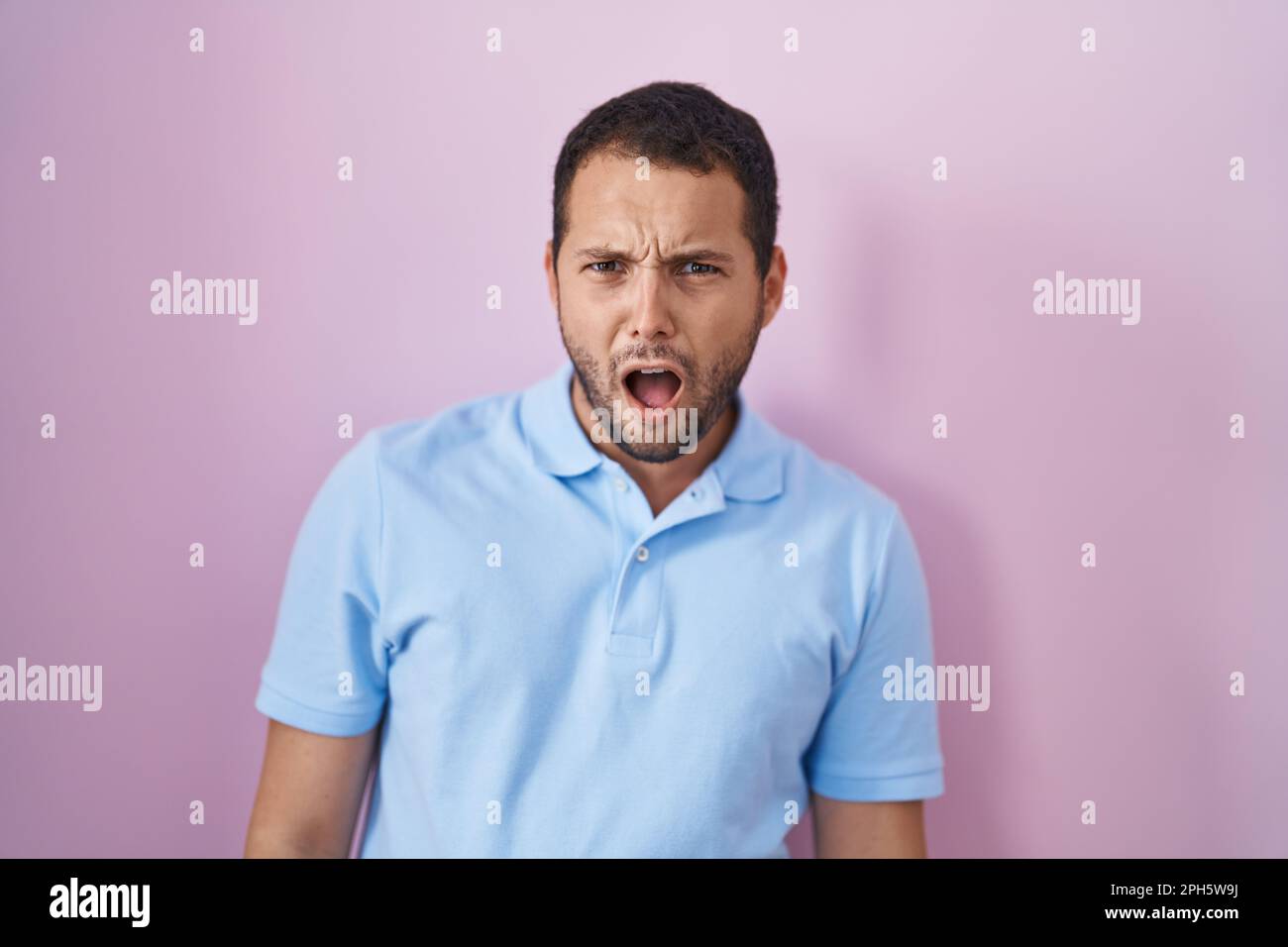 Hispanic man standing over pink background in shock face, looking ...