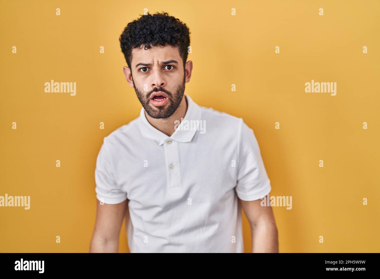 Arab man standing over yellow background in shock face, looking ...