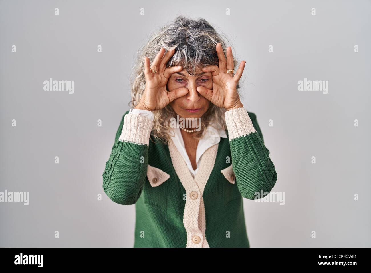 Middle age woman standing over white background trying to open eyes ...