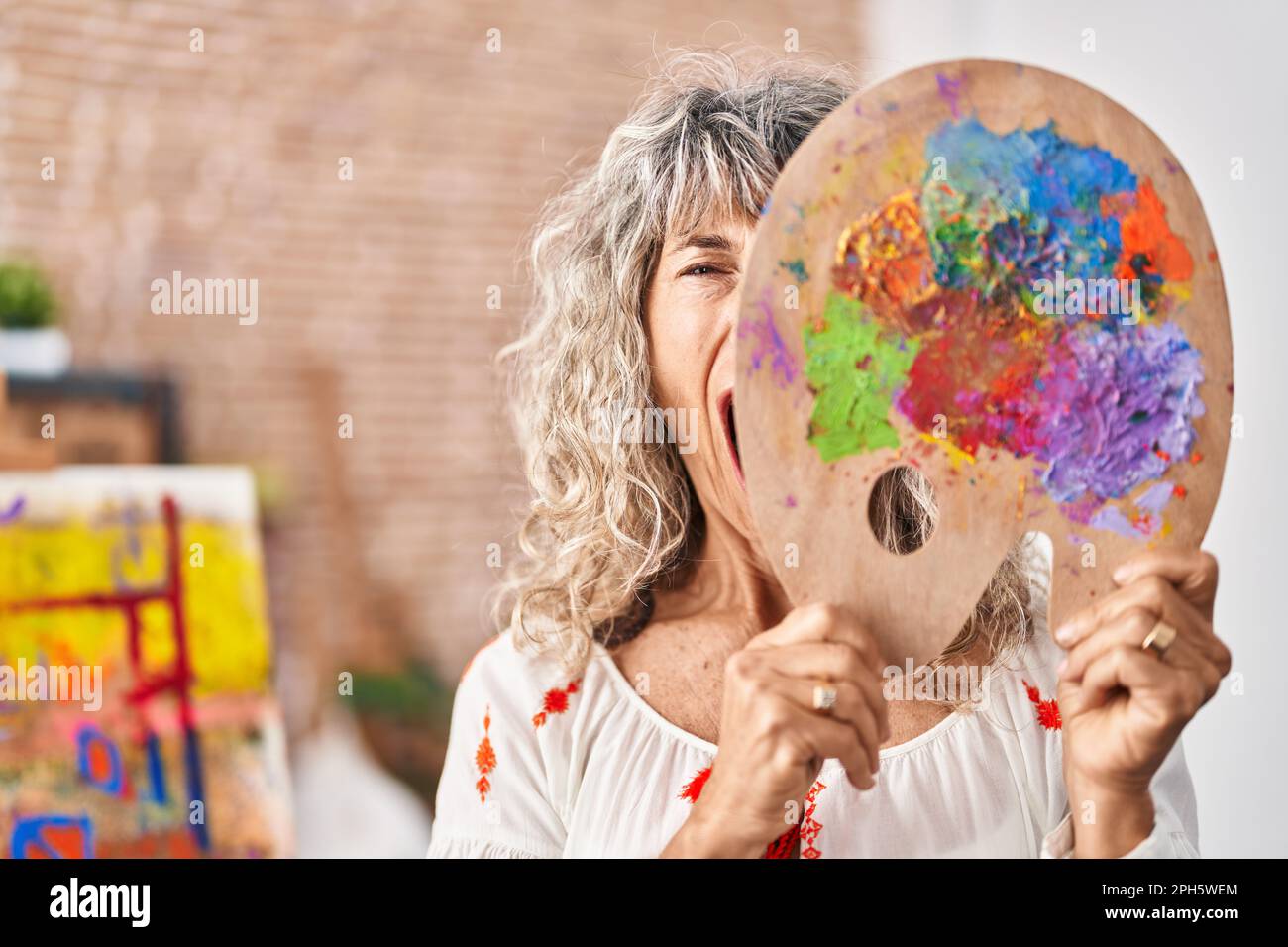 Middle age woman holding painter palette covering face angry and mad ...