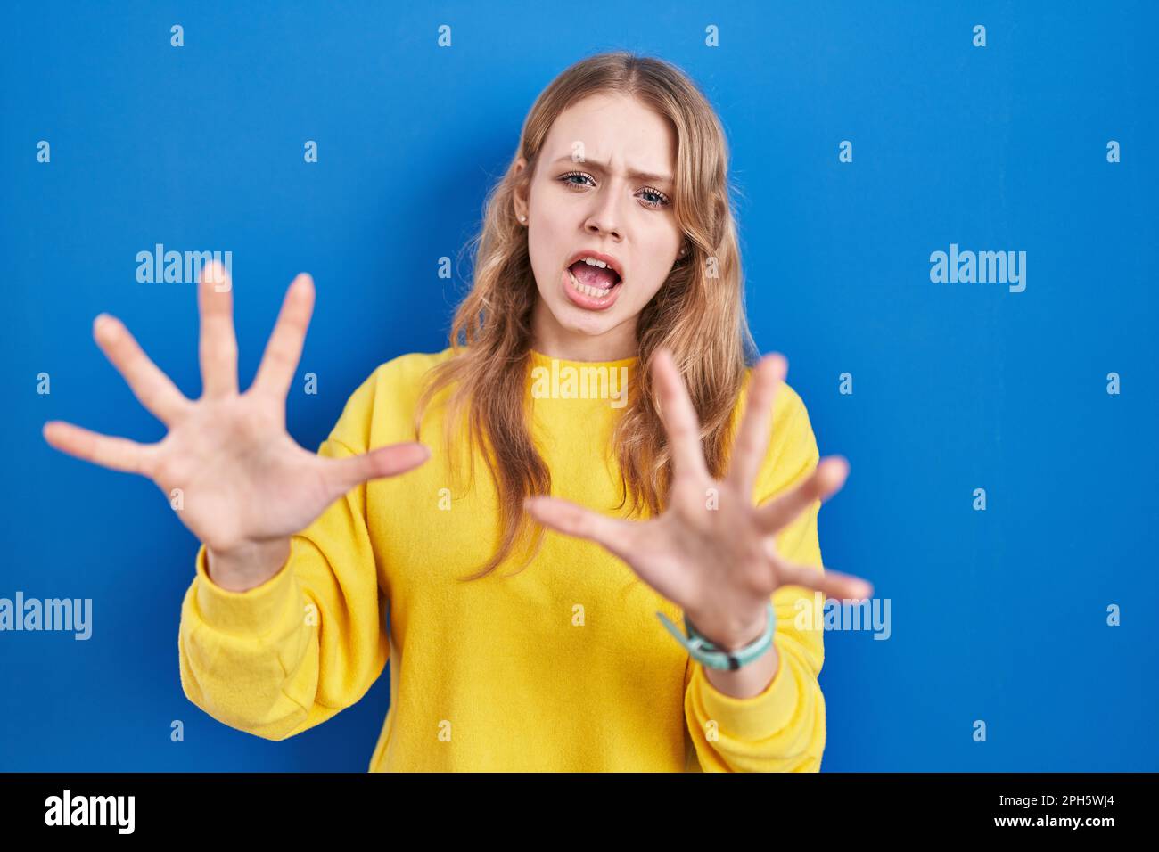 Young caucasian woman standing over blue background afraid and ...