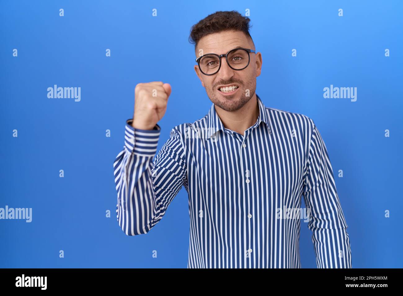 Hispanic man with beard wearing glasses angry and mad raising fist ...