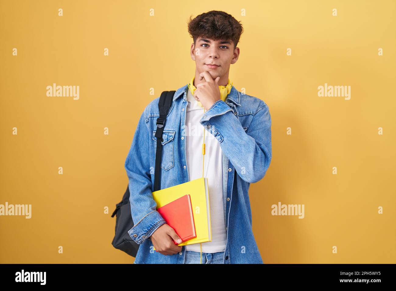 Hispanic teenager wearing student backpack and holding books looking ...