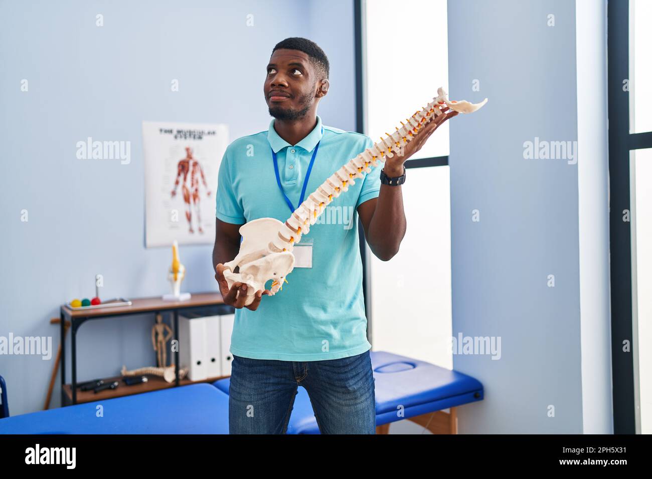African american man holding anatomical model of spinal column smiling ...