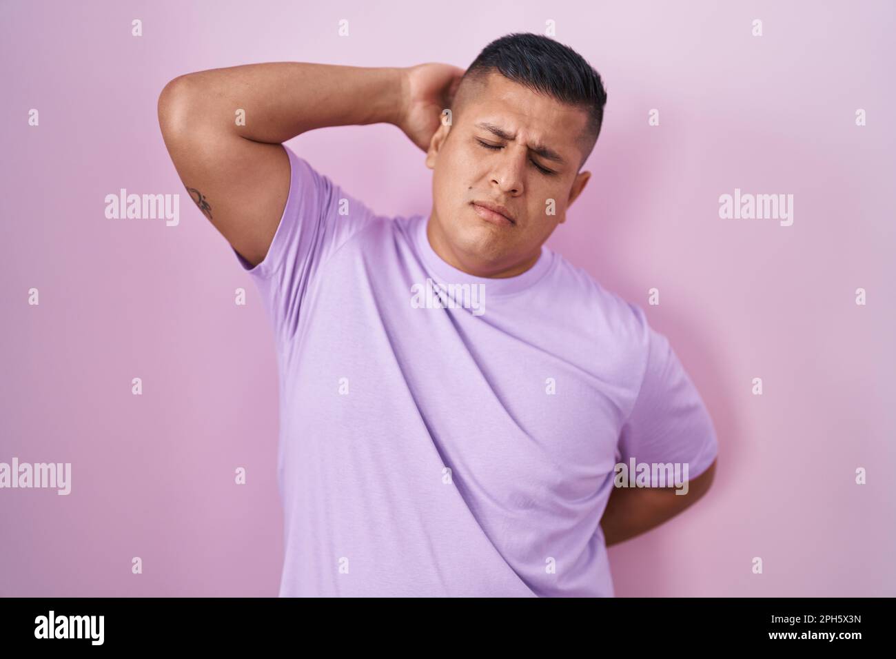 Young hispanic man standing over pink background suffering of neck ache ...
