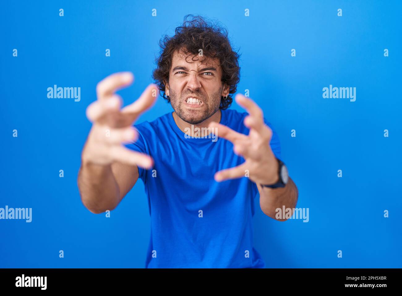 Hispanic young man standing over blue background shouting frustrated ...
