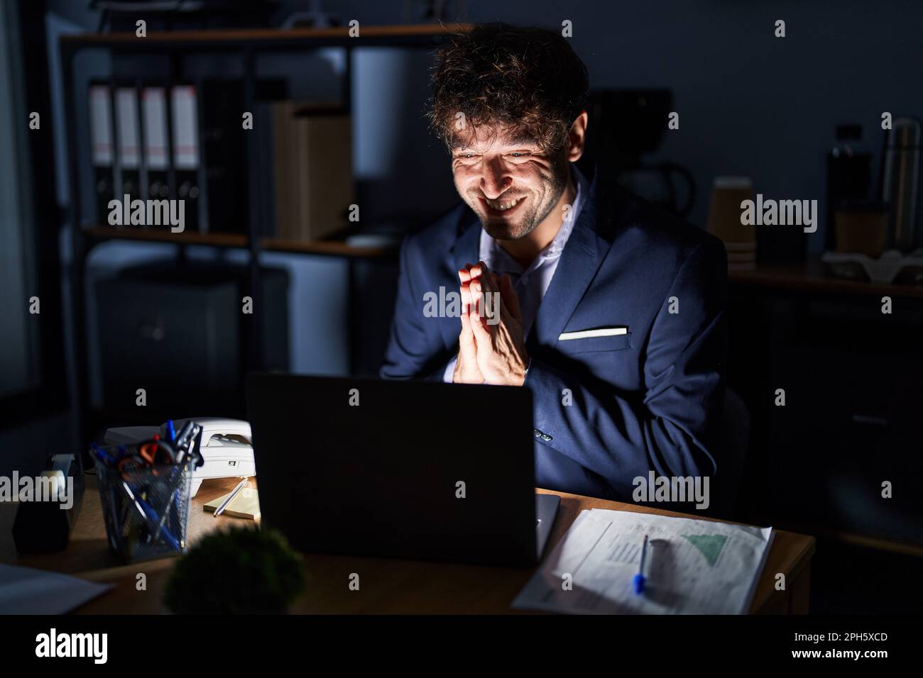 Hispanic young man working at the office at night praying with hands ...