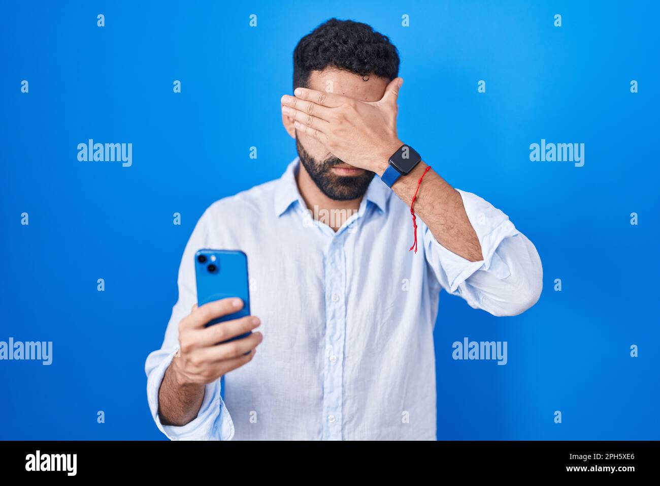 Hispanic Man With Beard Using Smartphone Typing Message Covering Eyes